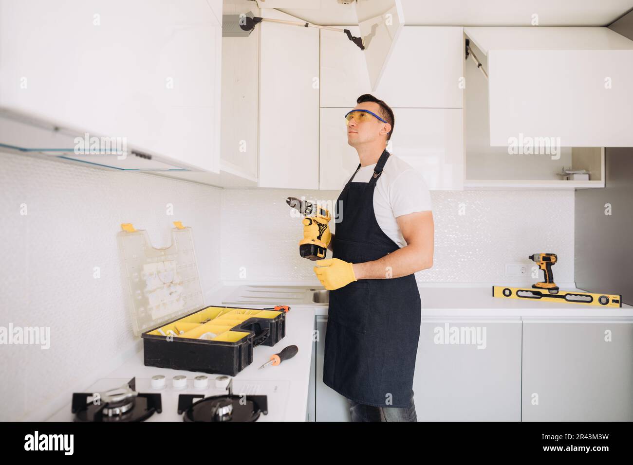 Maintenance man installing kitchen furniture in a black apron and ...