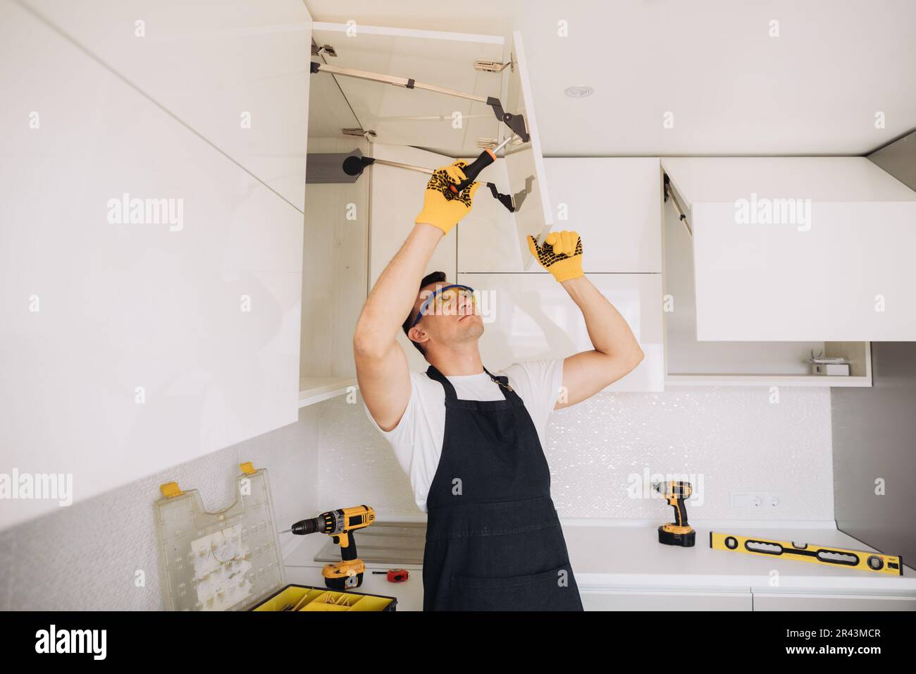 Maintenance man installing kitchen furniture in a black apron and ...
