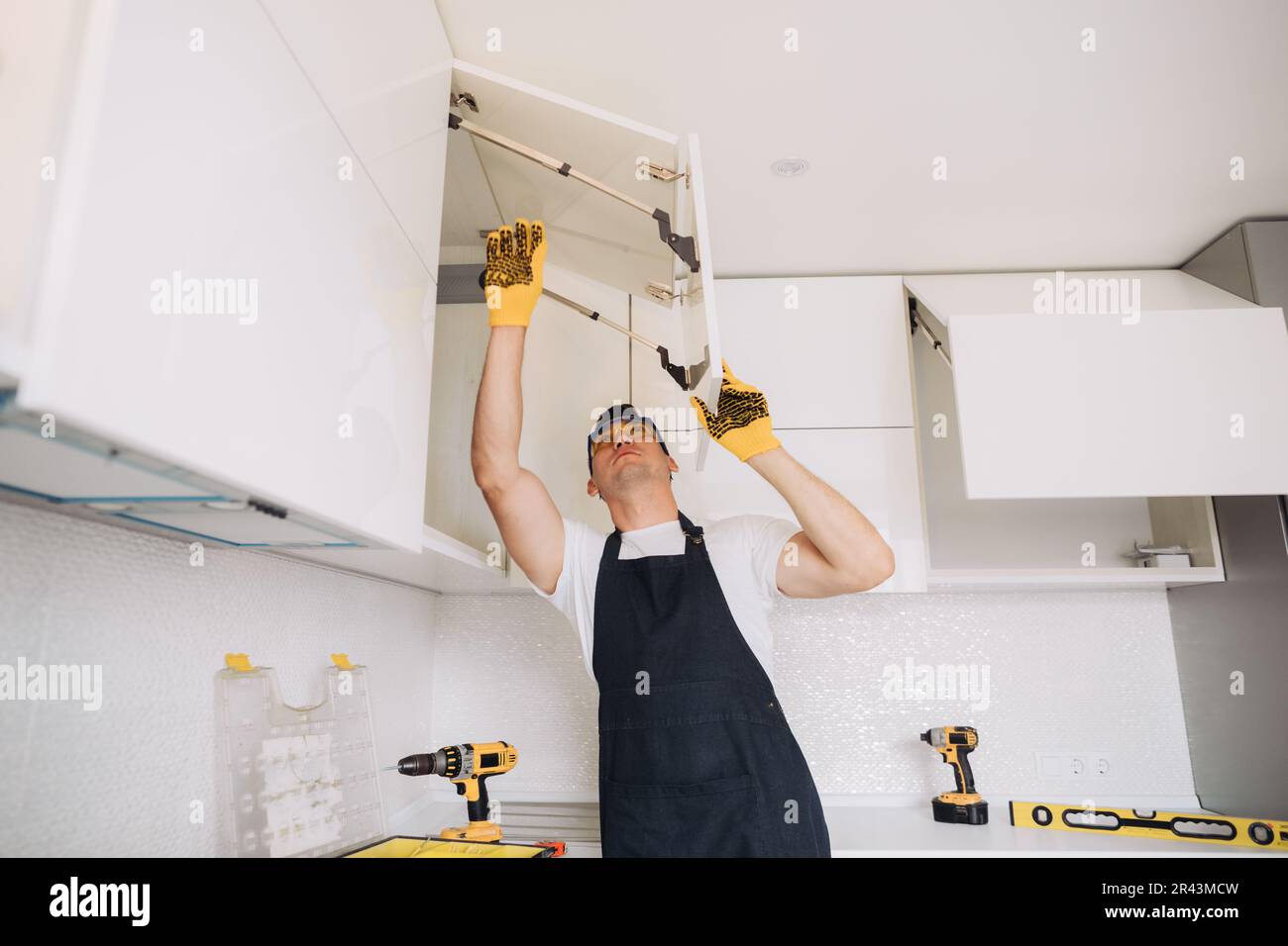 Maintenance man installing kitchen furniture in a black apron and ...