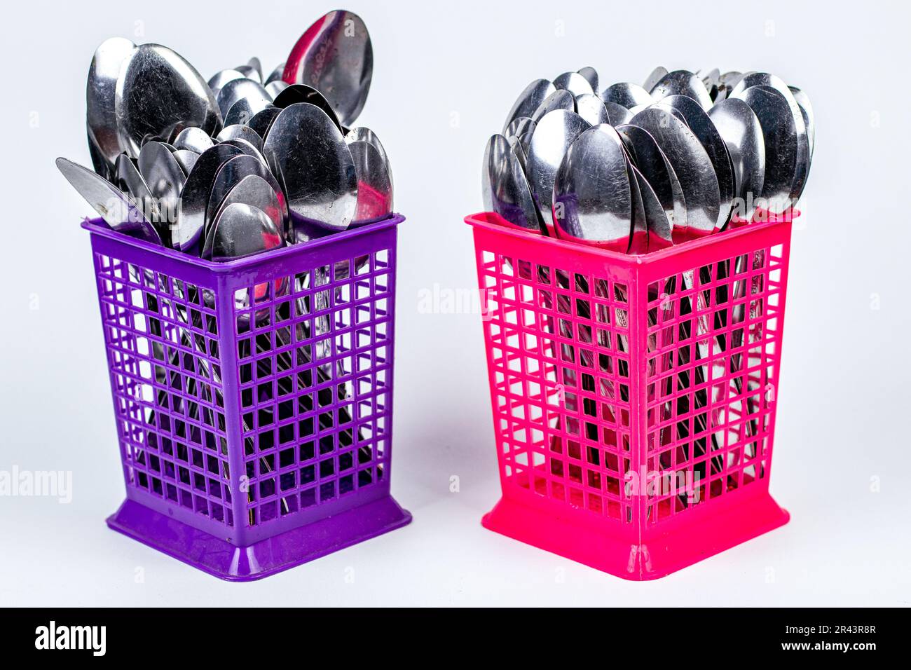 Stack of metal spoons in a pink plastic basket isolated on white ...