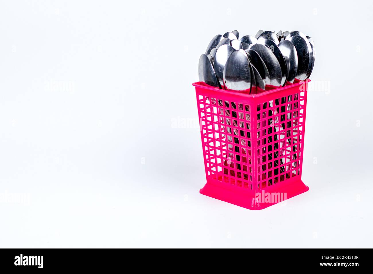 Stack of metal spoons in a pink plastic basket isolated on white ...