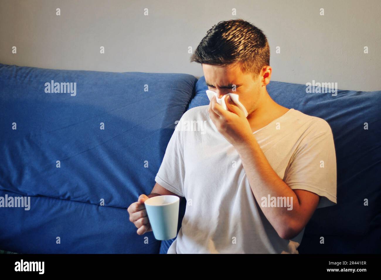 Cold man sitting on the couch with a handkerchief and a cup of tea ...