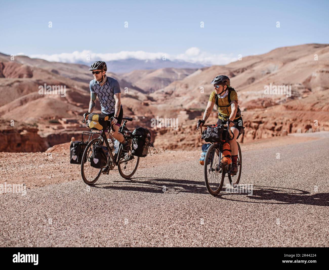 Two cyclists bike along remote mountain road in the desert of Morocco ...
