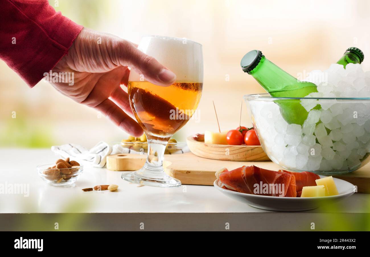Man picking up glass of beer on white table with appetizer in a kitchen ...