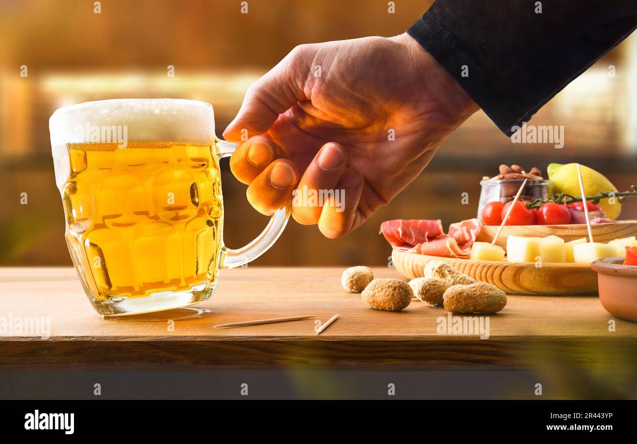 Man with a mug of beer in hand on wooden bench with appetizer prepared ...