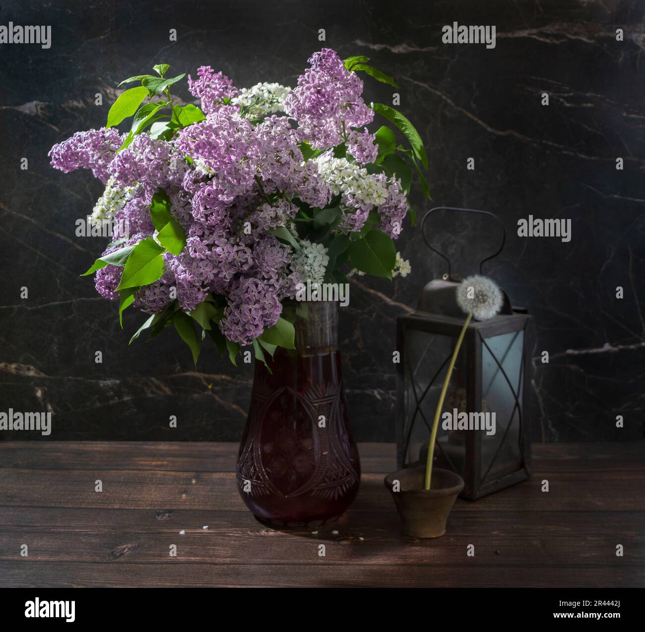 Still life with lilacs in a glass vase with a white dandelion and an ...