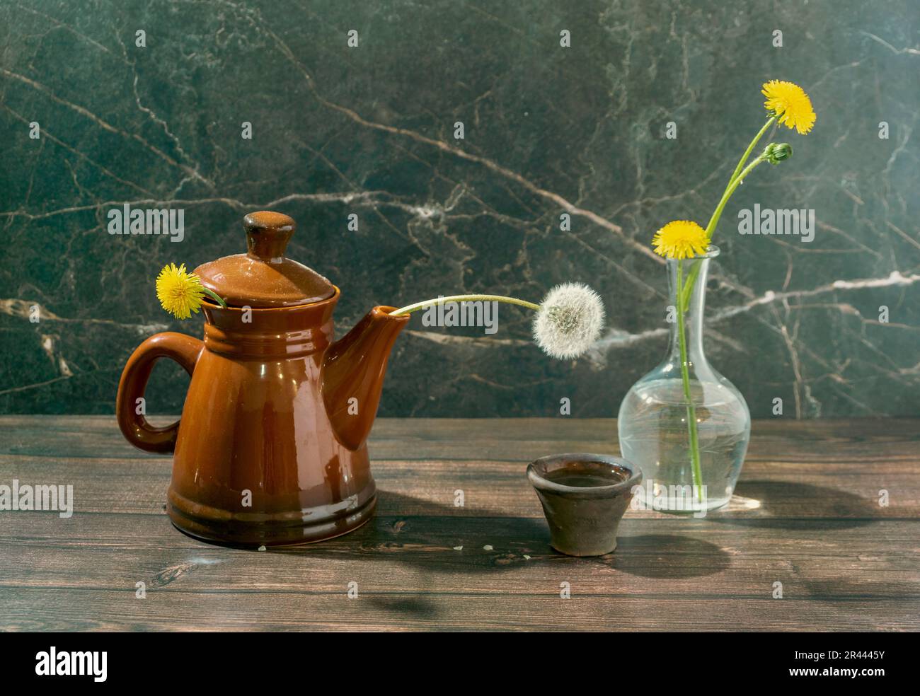 Still life with yellow dandelions in a teapot and a clear glass vase ...