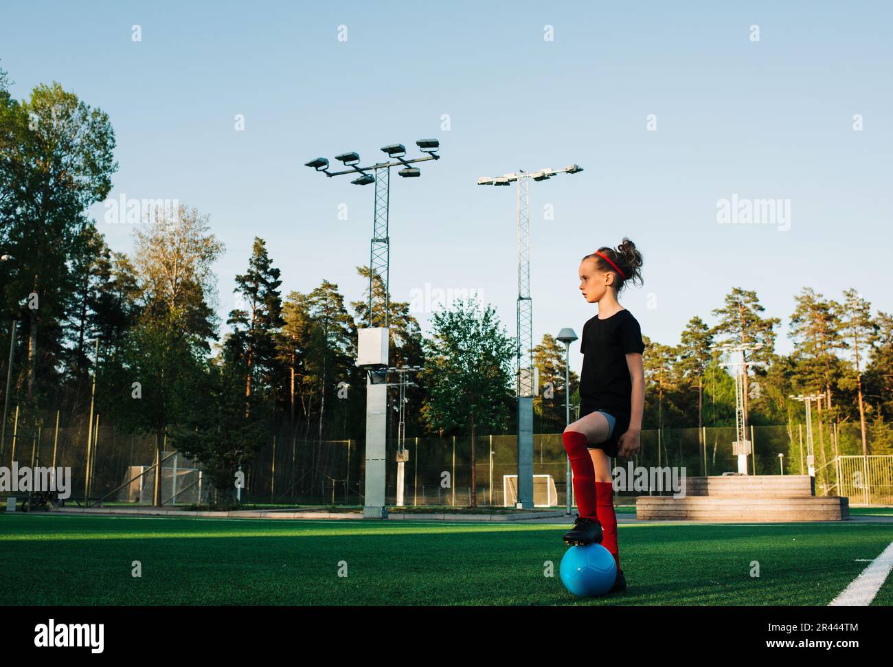 girl stood with her football boots on a ball in the middle of a pitch ...