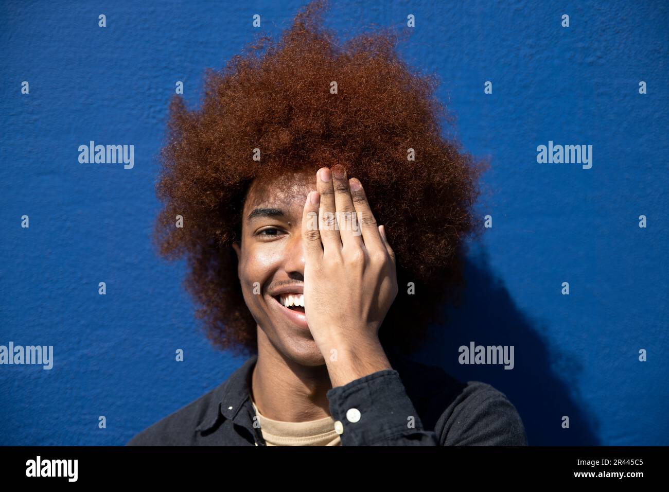 Close up of a happy smiling young man covering one eye with his hand ...