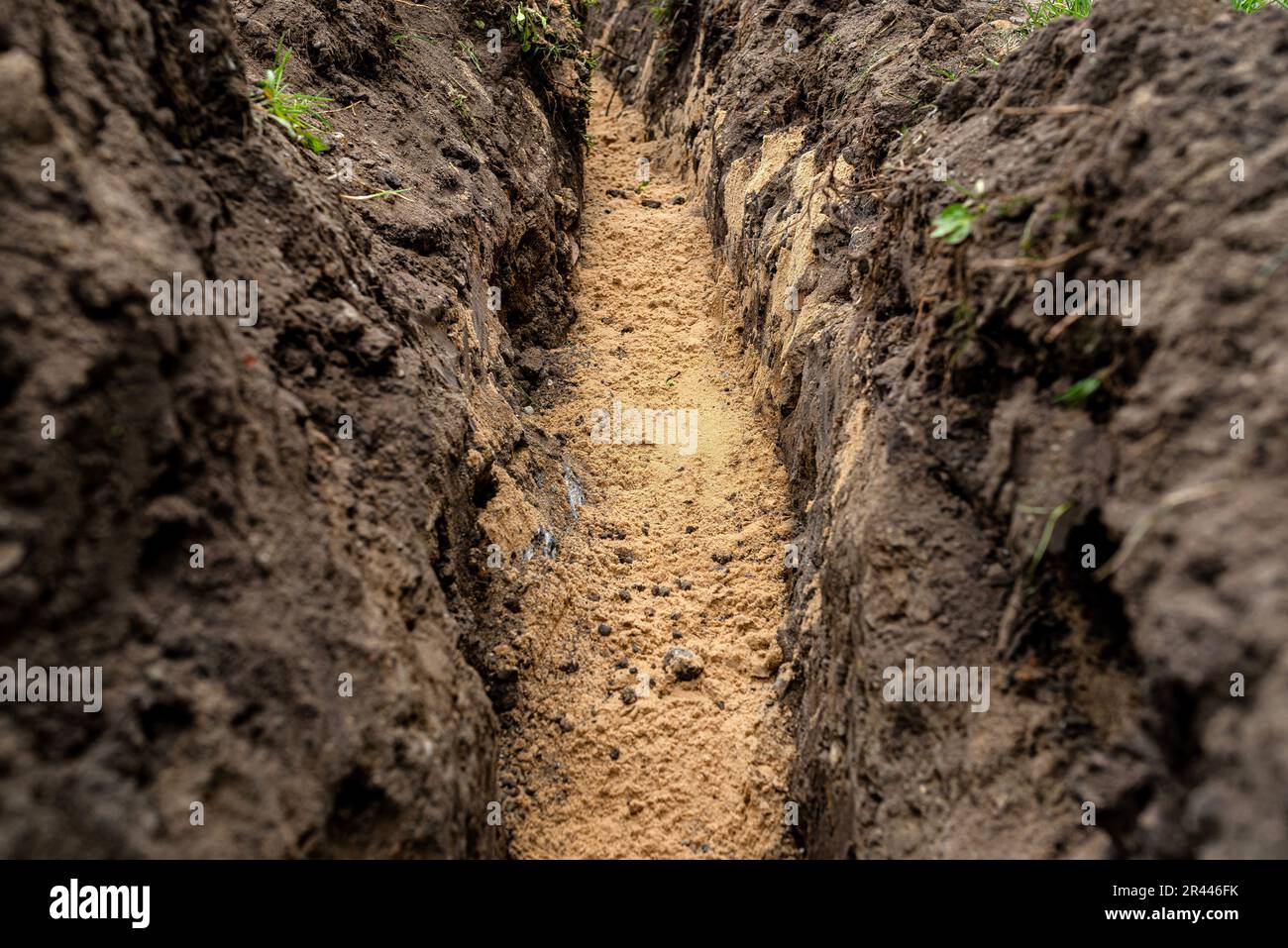 A trench dug in the yard along the fence to lay the drainage pipe ...