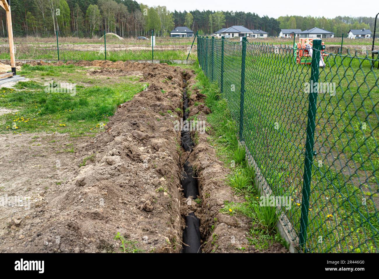 A trench dug in the yard along the fence to lay the drainage pipe ...