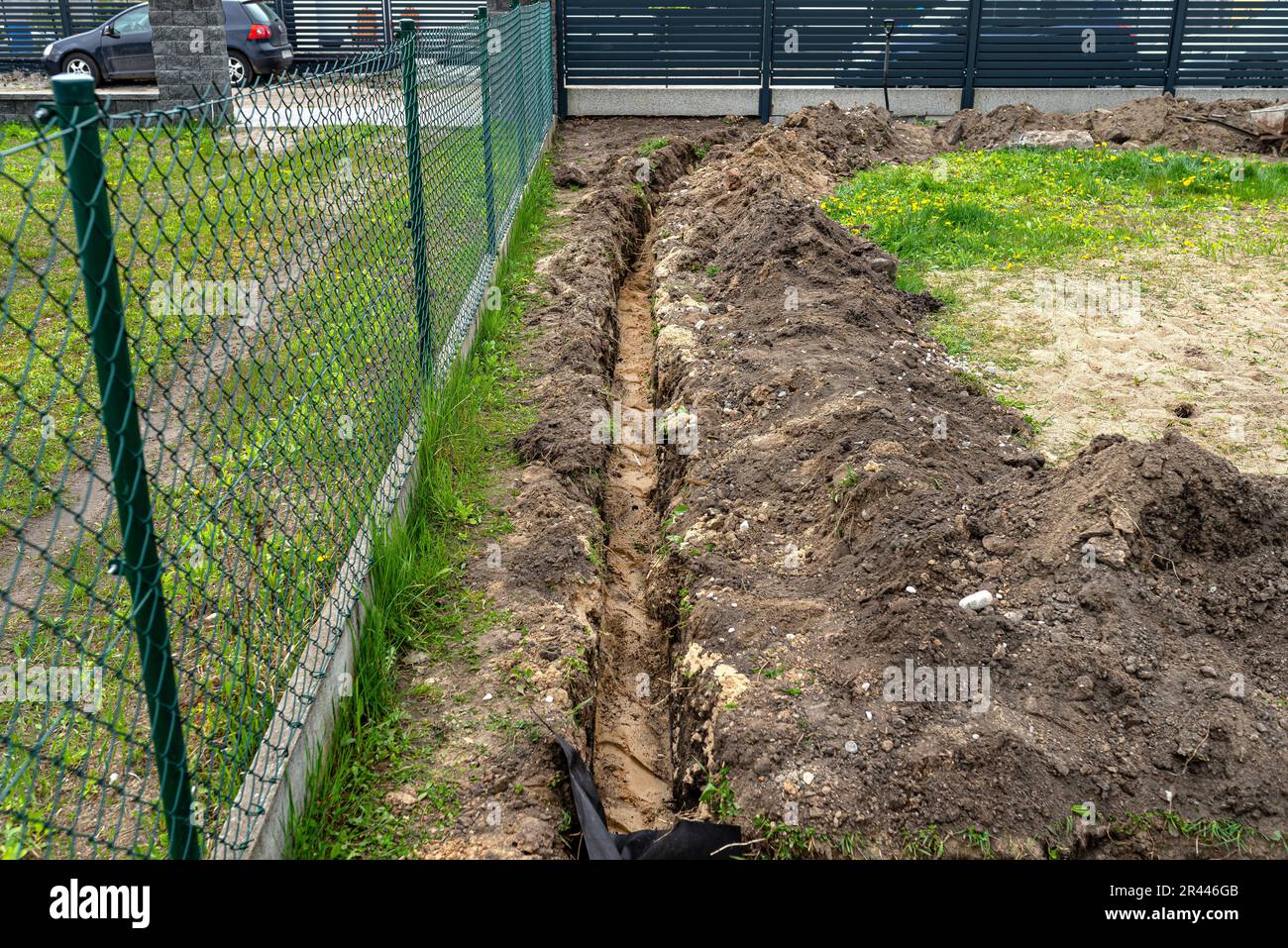 A trench dug in the yard along the fence to lay the drainage pipe ...