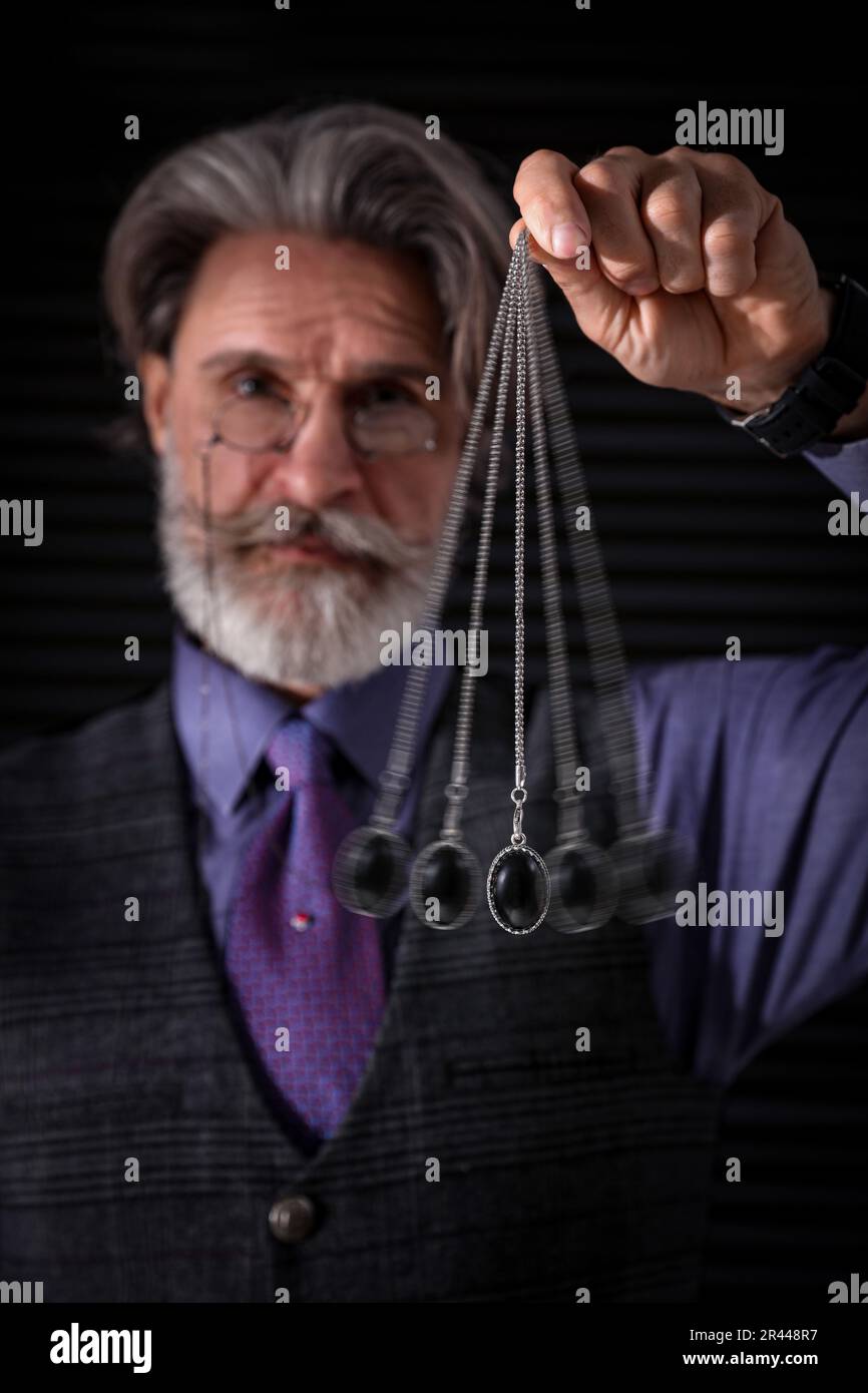 Hypnosis session. Man swinging pendant on black background, motion ...