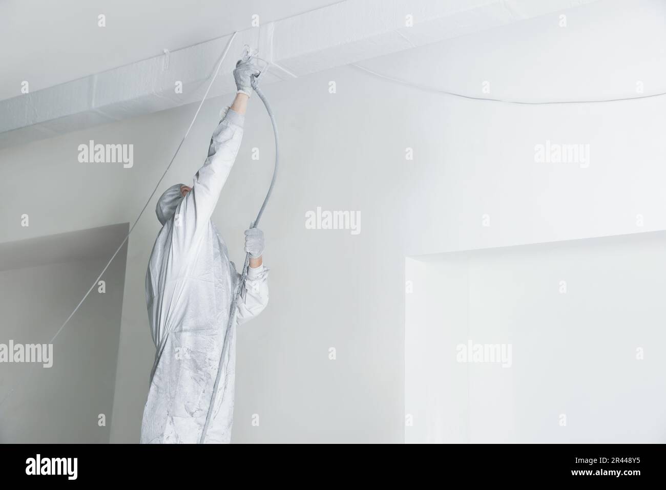 Decorator in protective overalls painting ceiling with spray gun ...