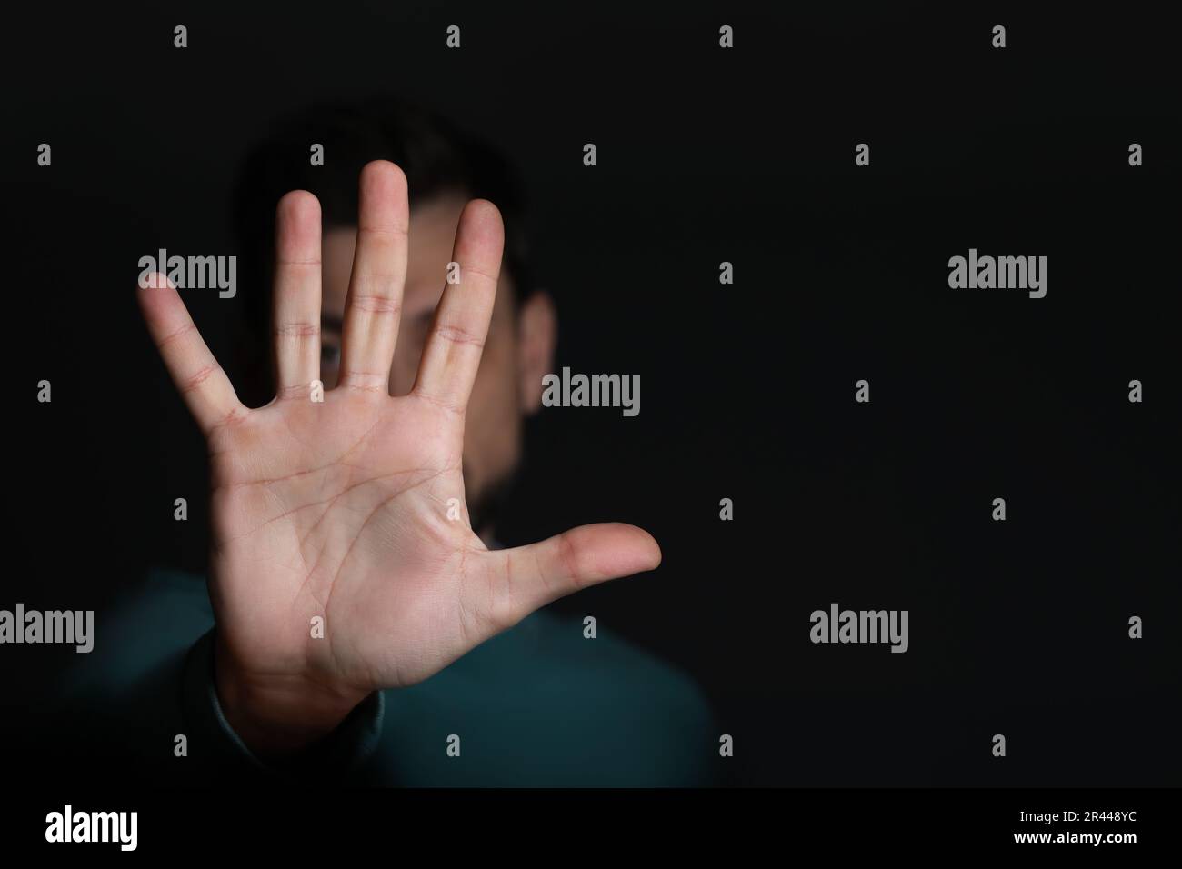 Man showing stop gesture against black background, focus on hand. Space ...