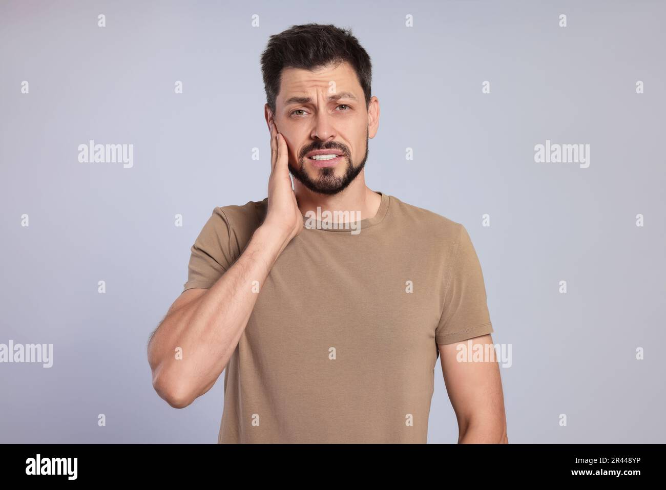Man suffering from ear pain on grey background Stock Photo - Alamy