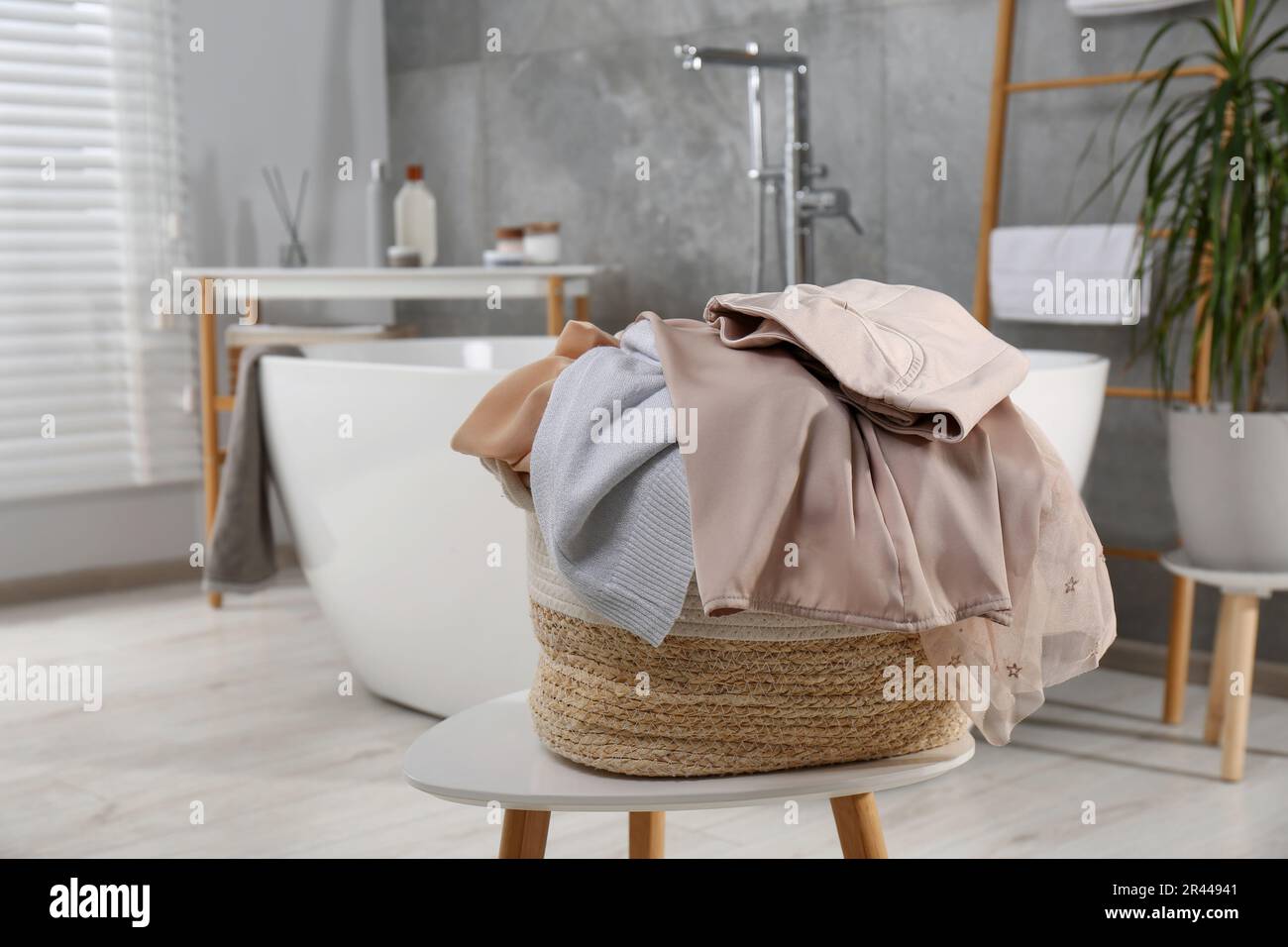 Wicker laundry basket with clothes on stool in bathroom Stock Photo - Alamy