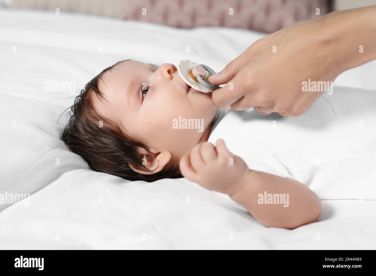 Mother giving pacifier to her little baby on bed, closeup Stock Photo ...