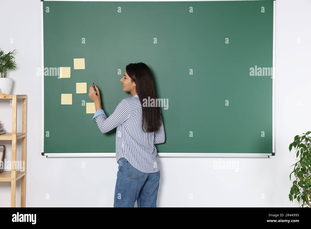 Happy young teacher giving lesson at blackboard in classroom. Space for ...