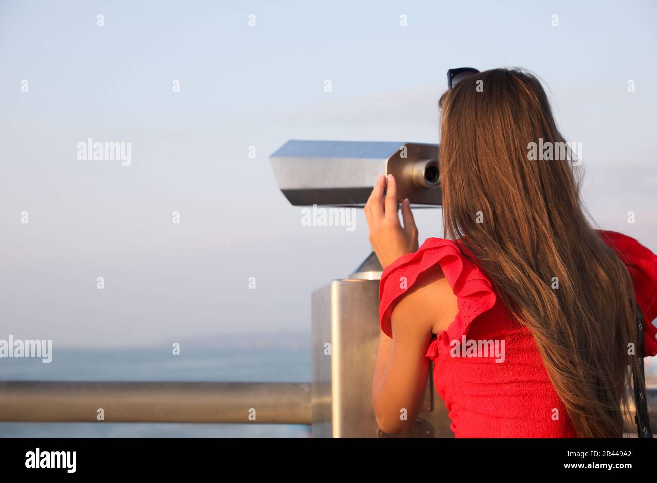 Young woman looking through tourist viewing machine at observation deck ...