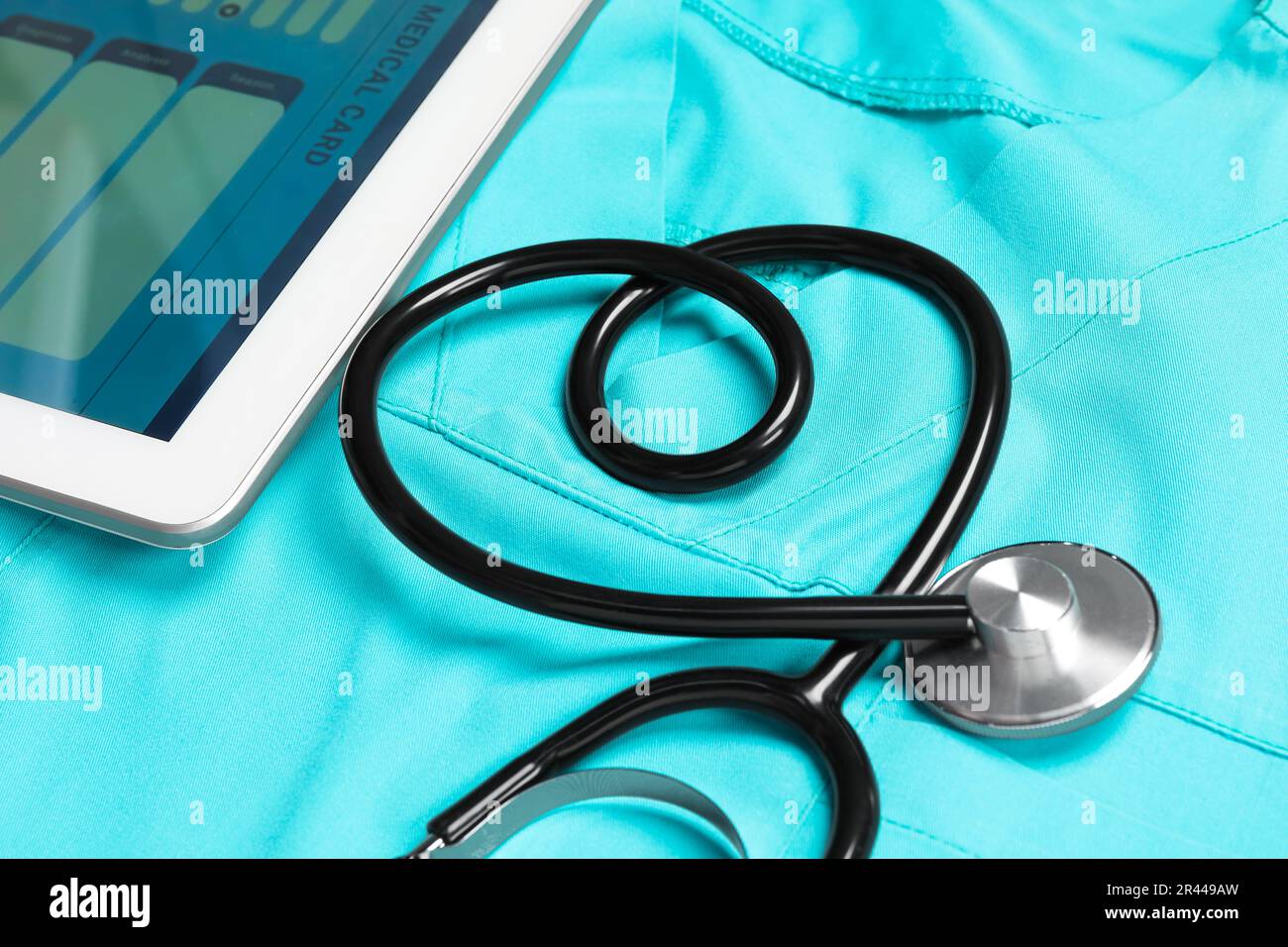 Stethoscope in shape of heart and tablet on turquoise medical uniform ...