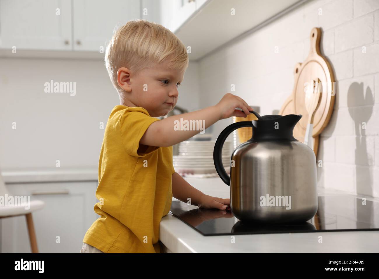 Curious little boy playing with kettle on electric stove in kitchen ...