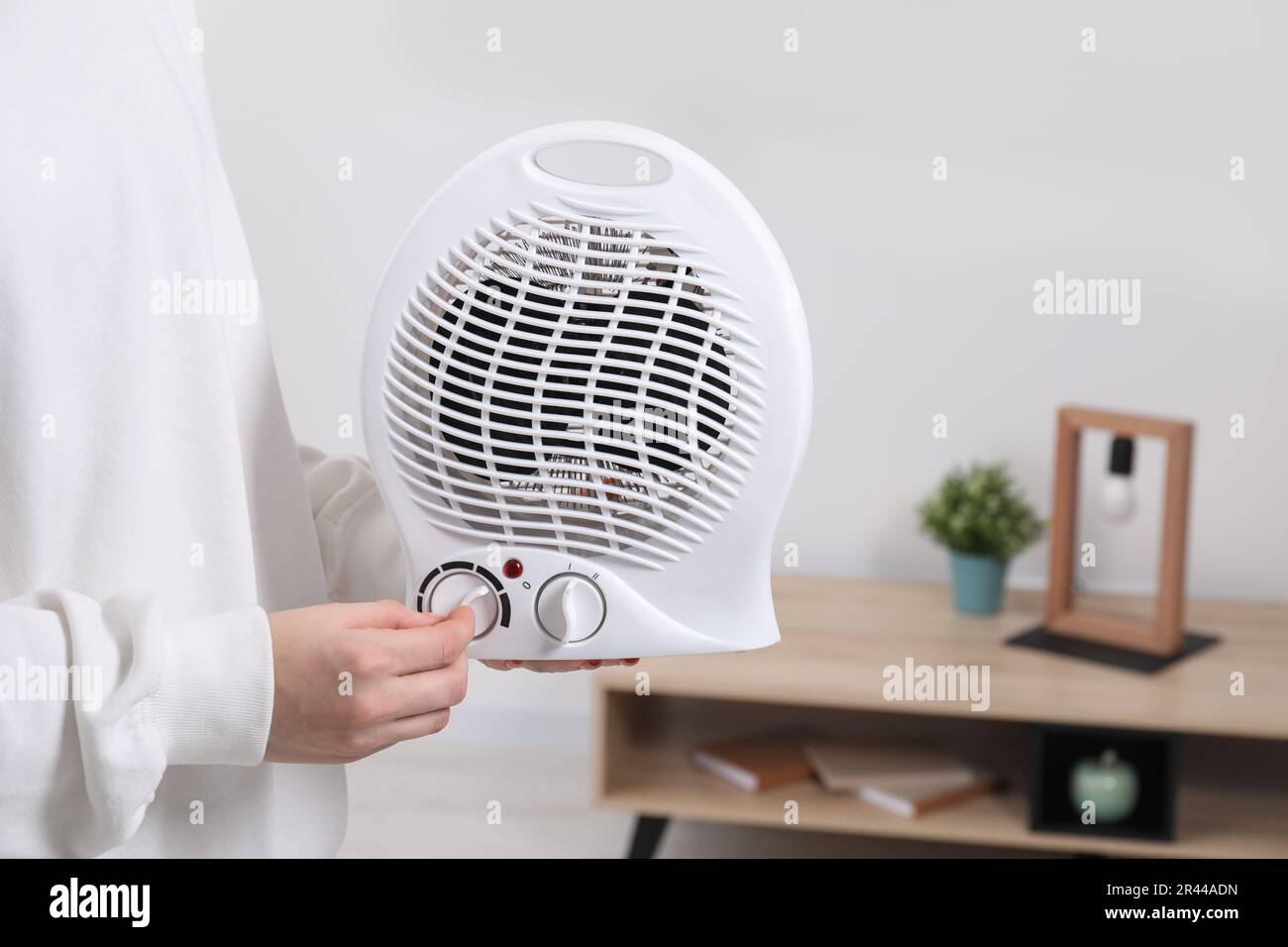 Woman turning on electric fan heater at home, closeup. Space for text ...