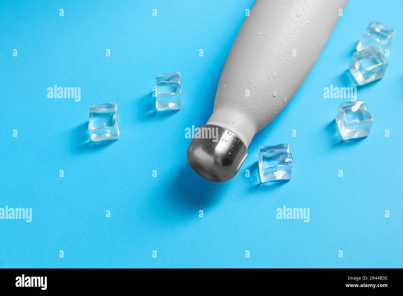 Stylish thermo bottle with water drops and ice cubes on light blue ...