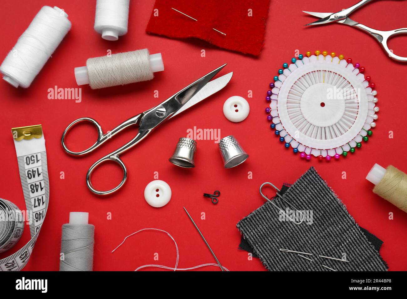 Flat lay composition with thimbles and different sewing tools on red ...