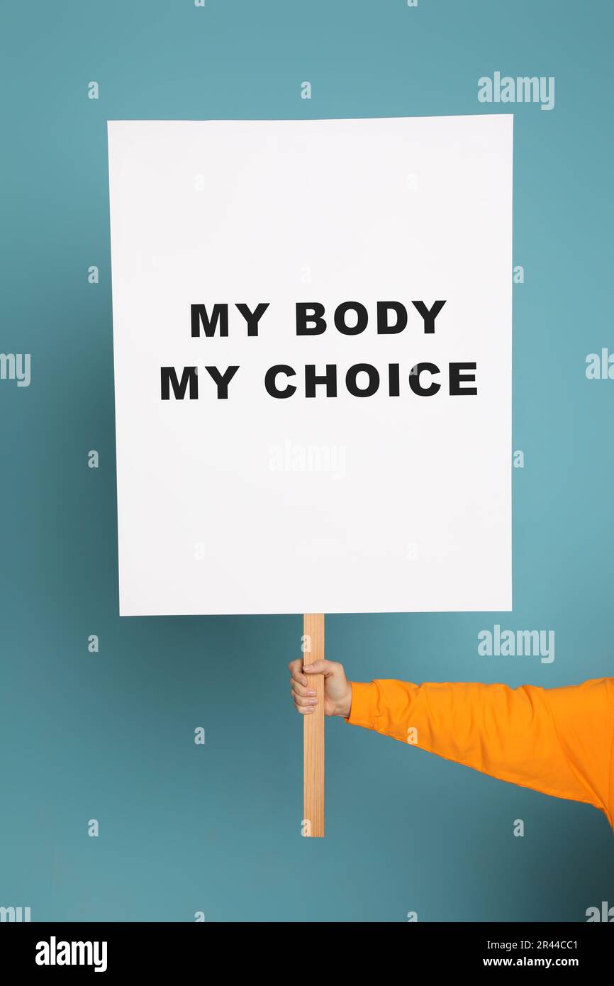 Woman holding placard with phrase My Body My Choice on light blue ...