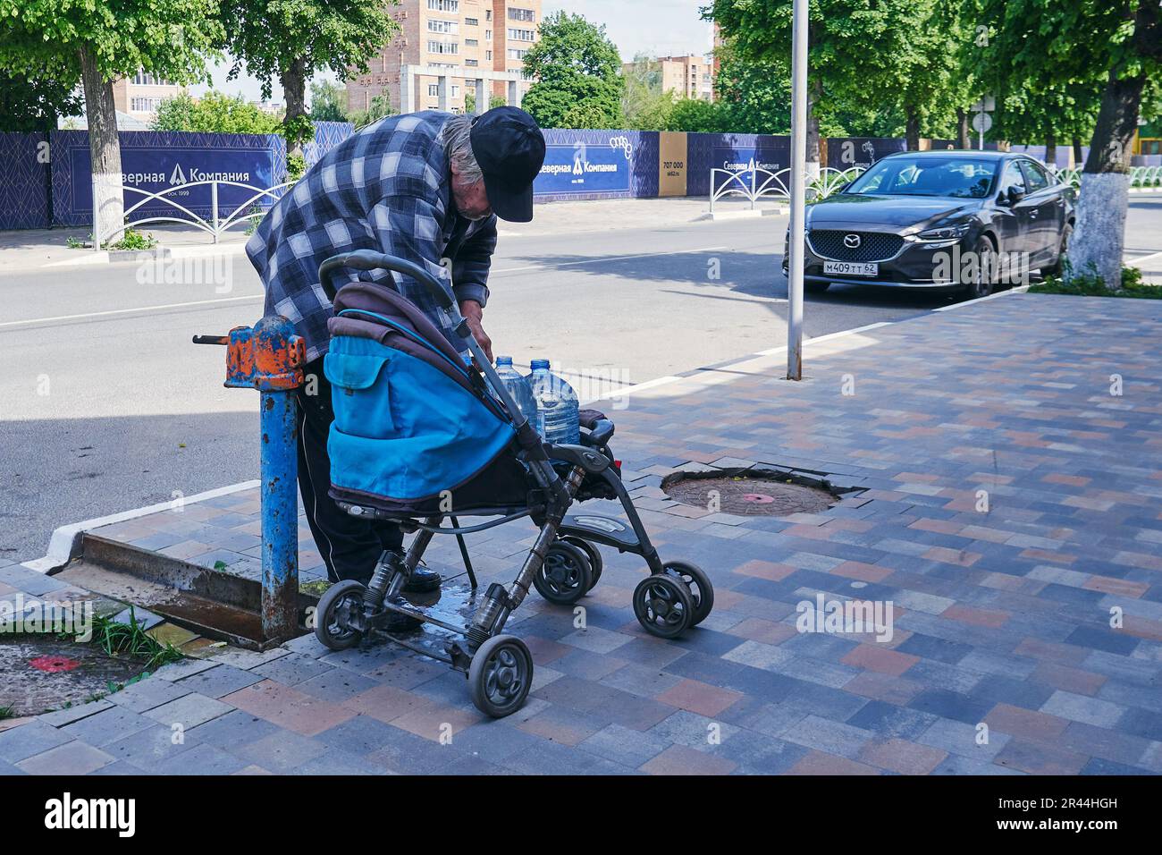 A homeless man transports water in a baby stroller. The old man made a ...