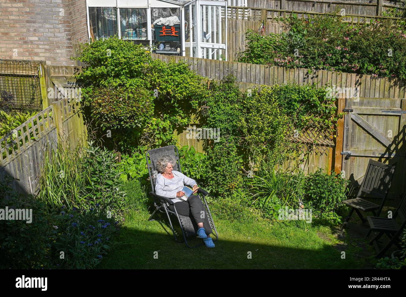 Woman sunbathing in a small urban garden reading a book in Brighton UK ...