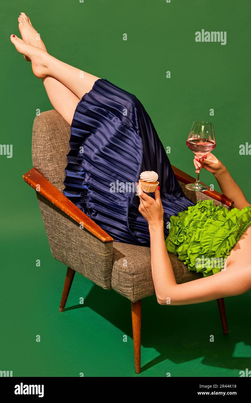 Woman lying on armchair, drinking rose wine and eating sweet muffin ...