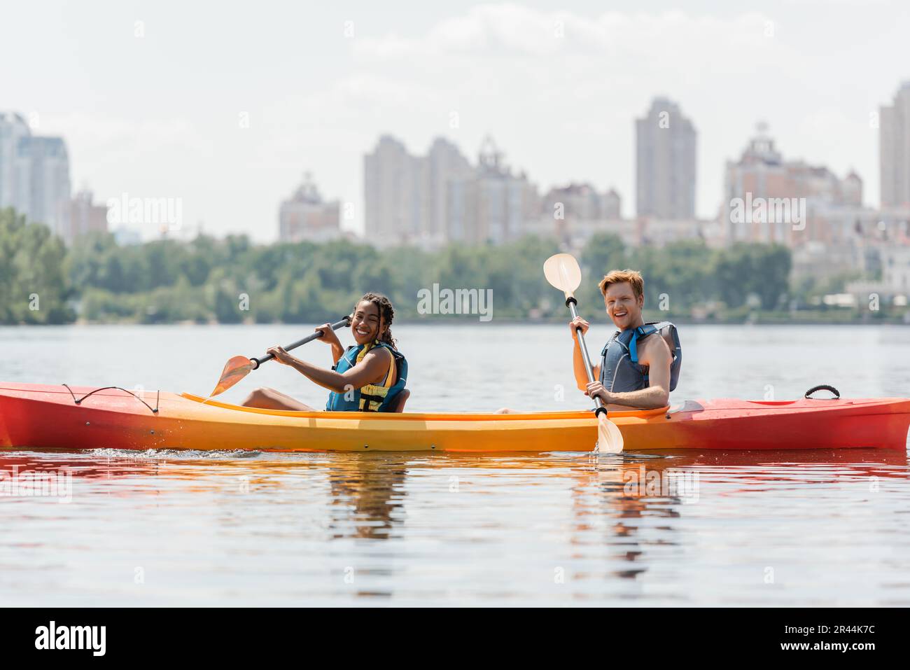 positive and sportive interracial couple in life vests sitting with ...