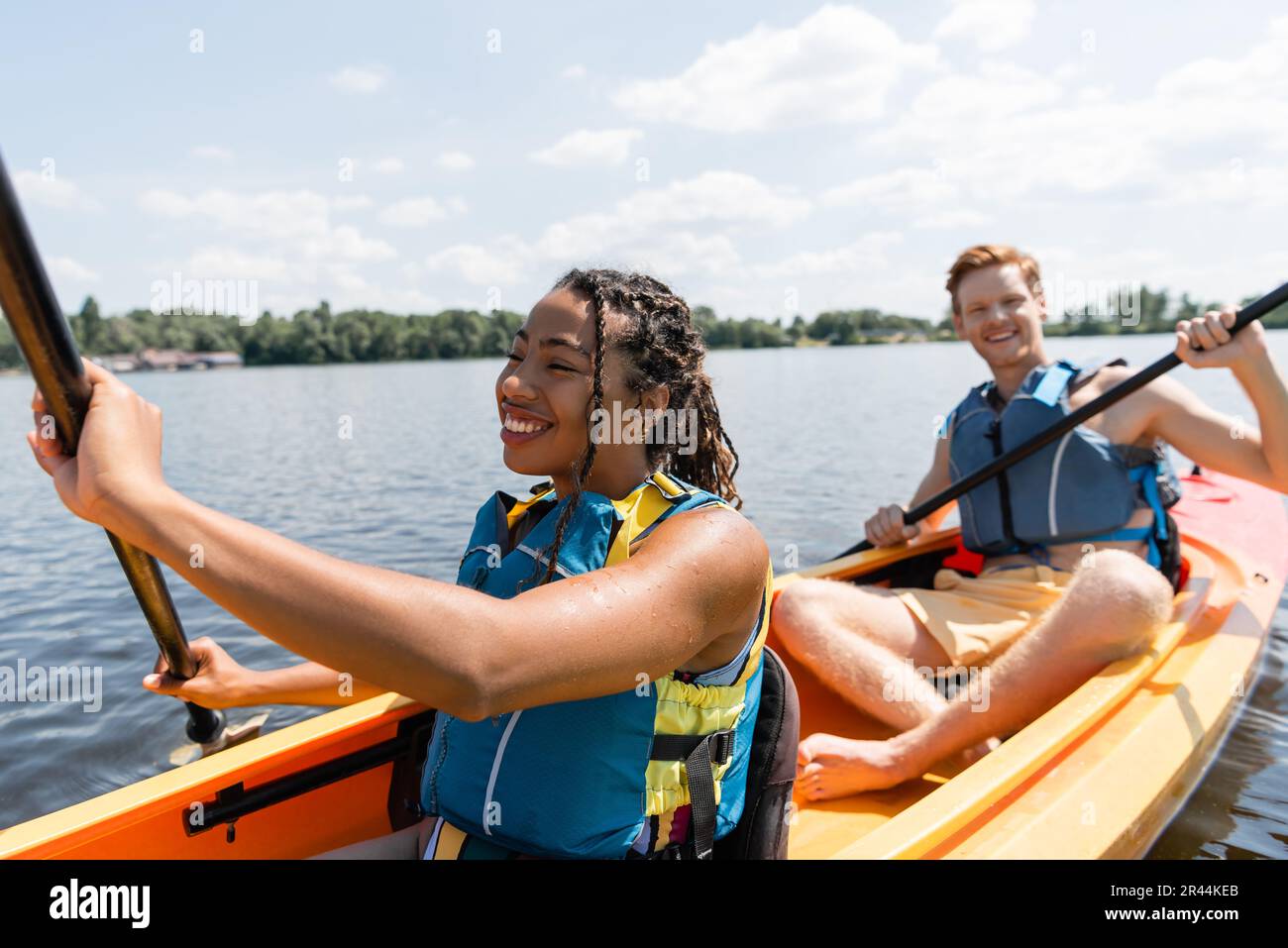 cheerful african american woman in life vest sailing in kayak while ...