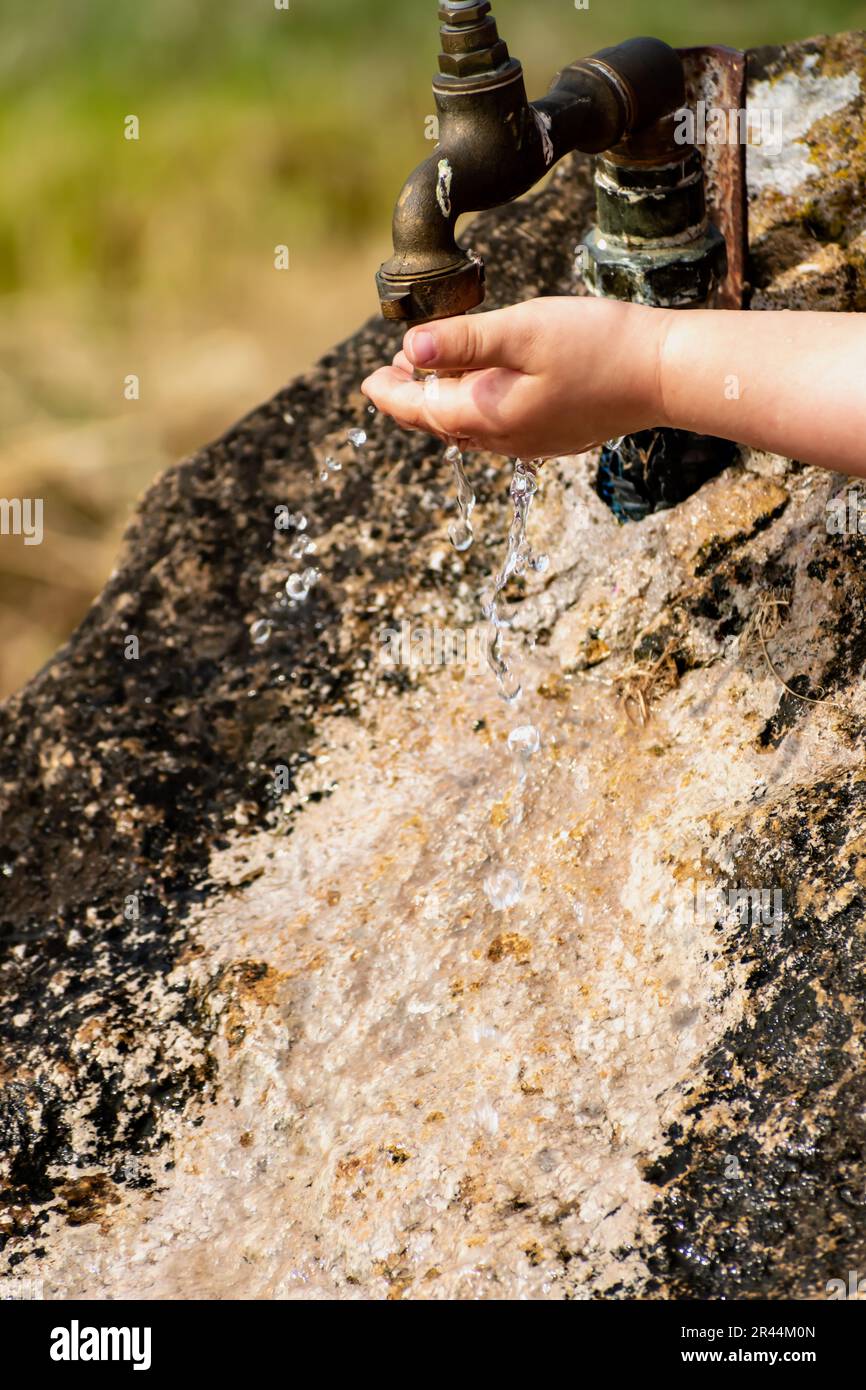 Baby cleaning his hands at an outdoor tap coming out of a stone ...