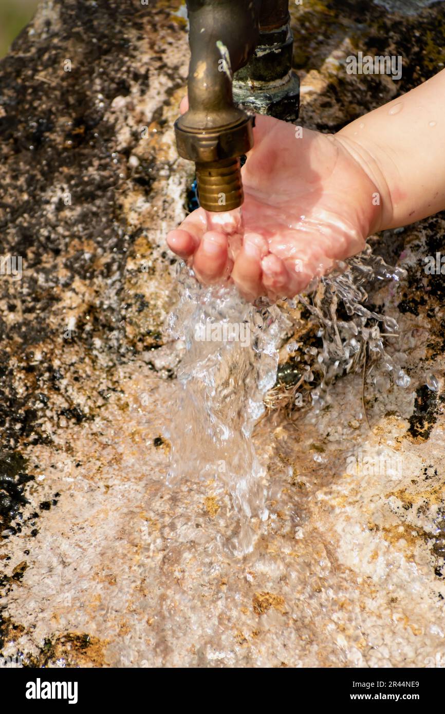 Baby cleaning his hands at an outdoor tap coming out of a stone ...