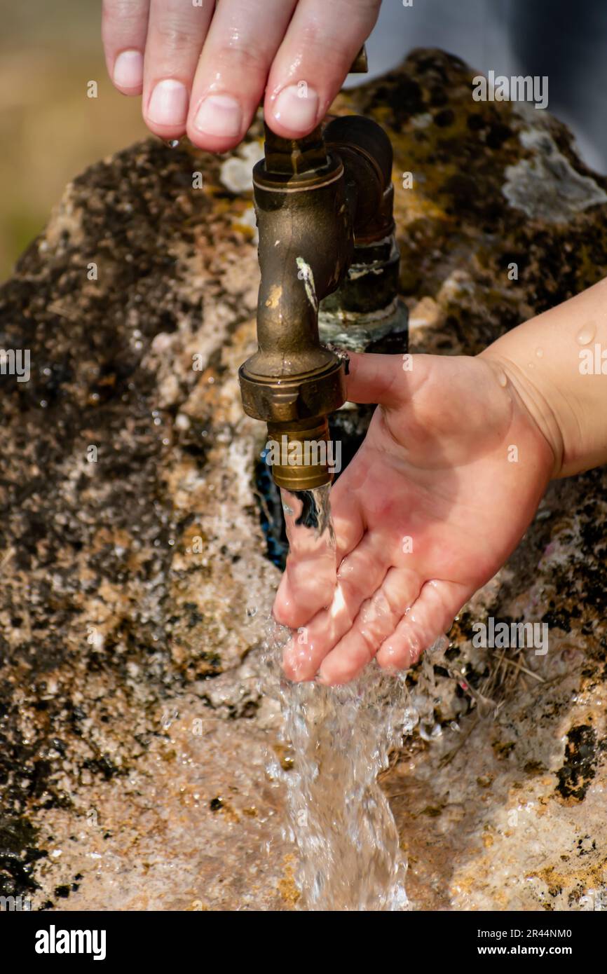 Baby cleaning his hands at an outdoor tap coming out of a stone ...