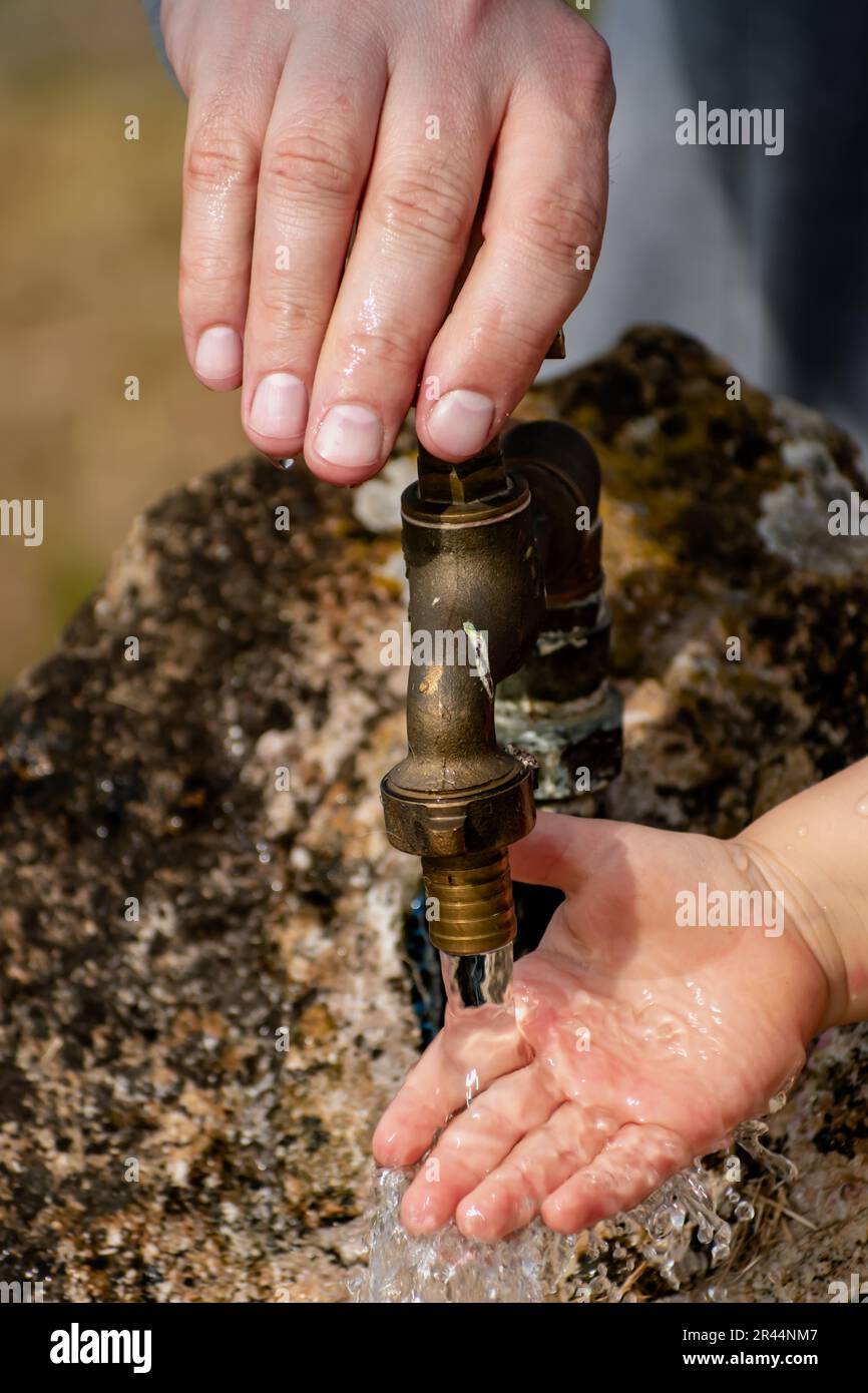 Baby cleaning his hands at an outdoor tap coming out of a stone ...