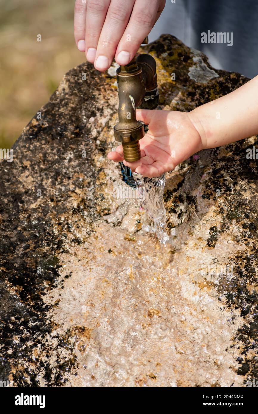 Baby cleaning his hands at an outdoor tap coming out of a stone, refreshing splashes without ...