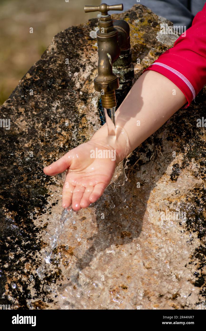 Baby cleaning his hands at an outdoor tap coming out of a stone ...