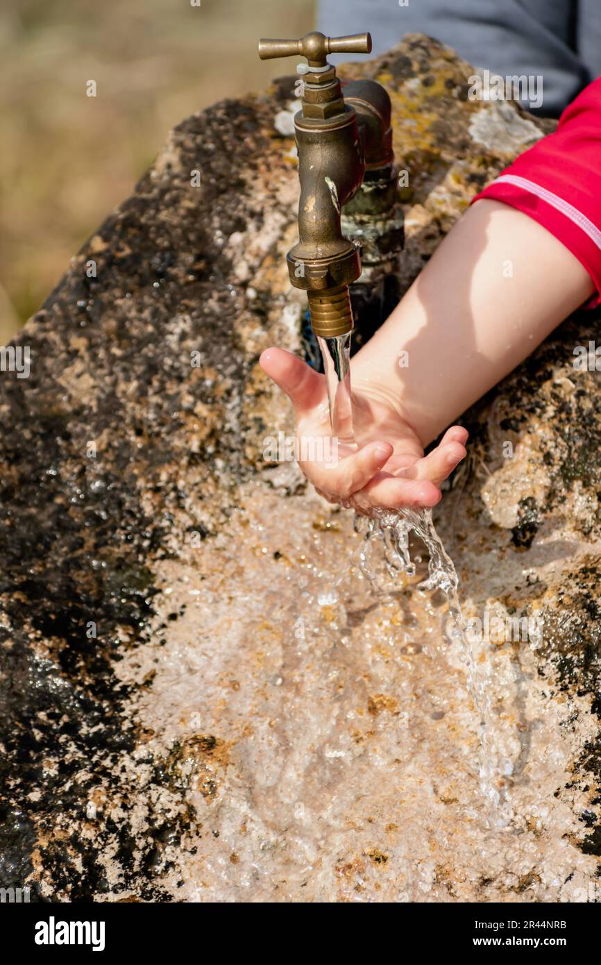 Baby cleaning his hands at an outdoor tap coming out of a stone ...