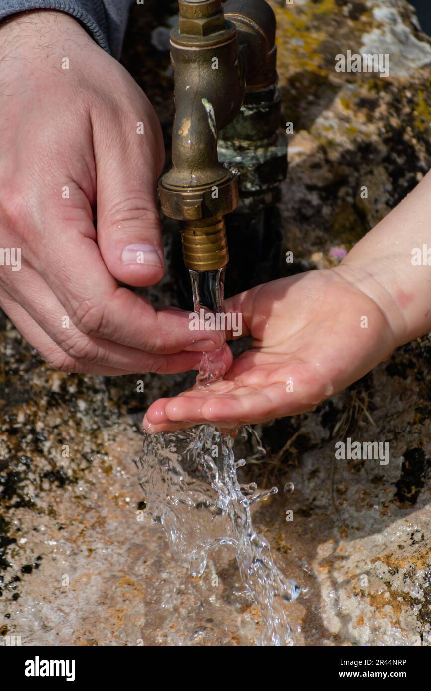 Baby cleaning his hands at an outdoor tap coming out of a stone ...