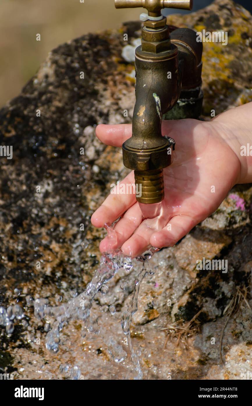 Baby cleaning his hands at an outdoor tap coming out of a stone ...