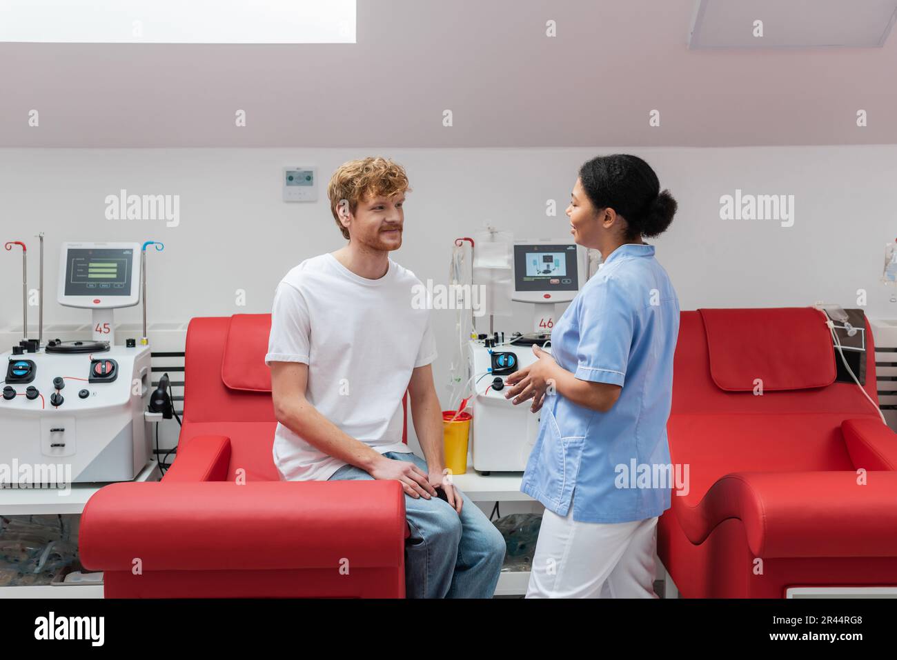 multiracial nurse in uniform talking to positive redhead volunteer ...