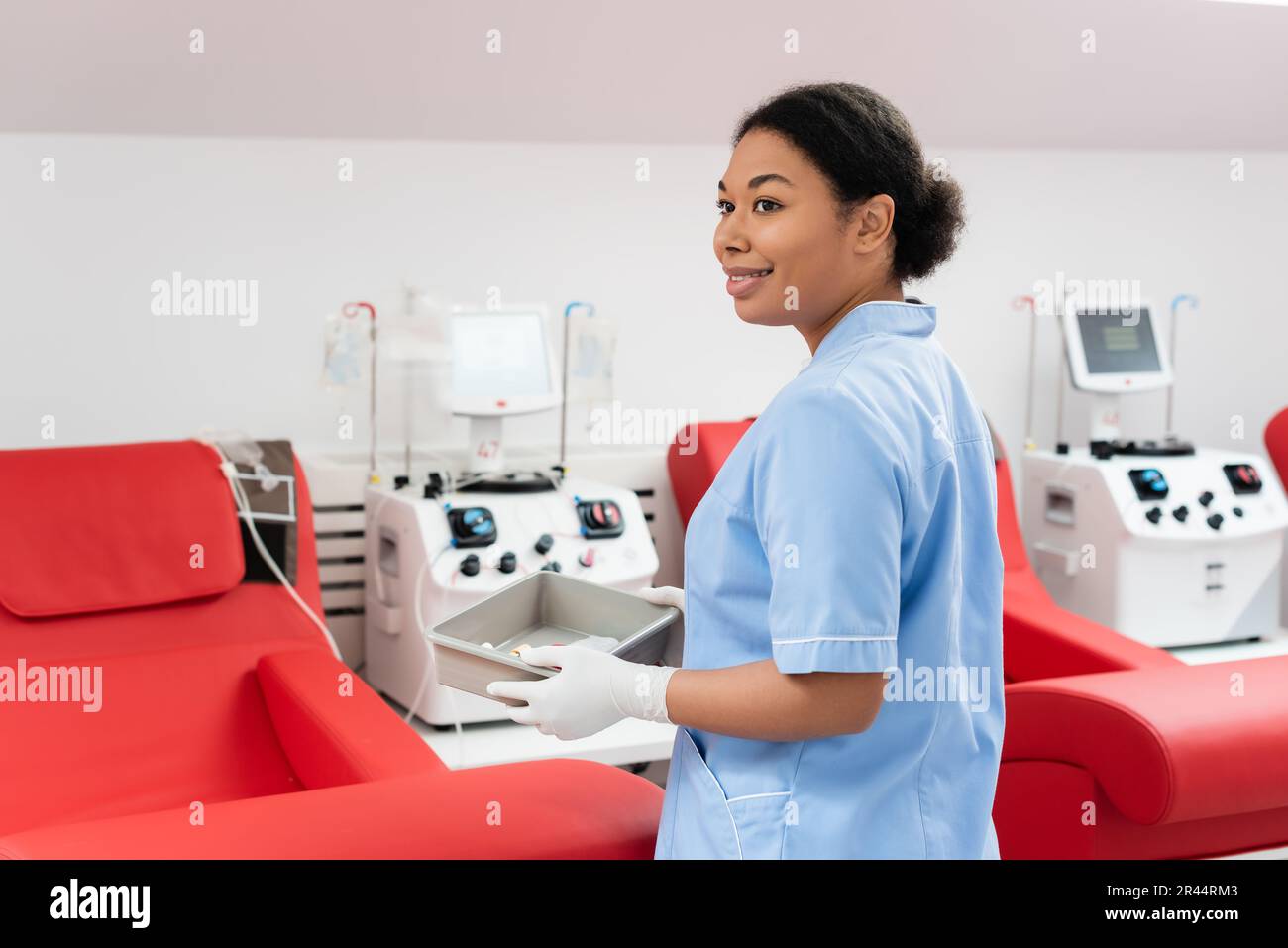 smiling multiracial nurse in blue uniform and latex gloves holding ...