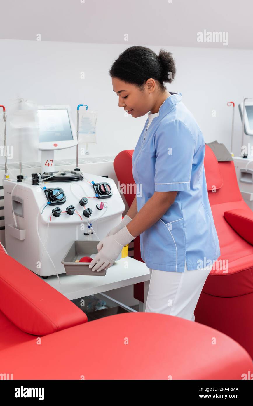 side view of multiracial nurse in uniform and latex gloves holding ...