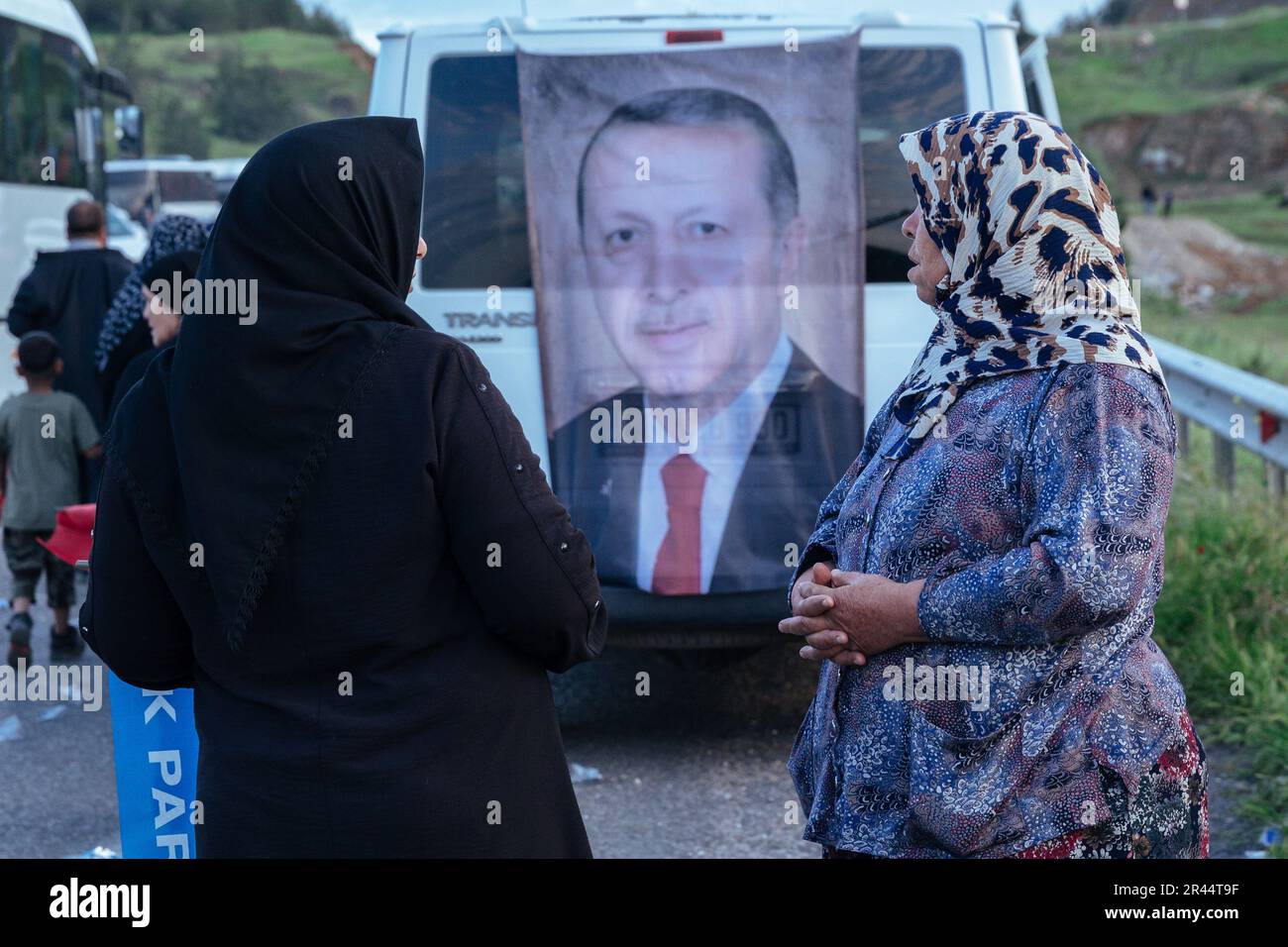 Two women seen standing in front of a flag with the portrait of ...