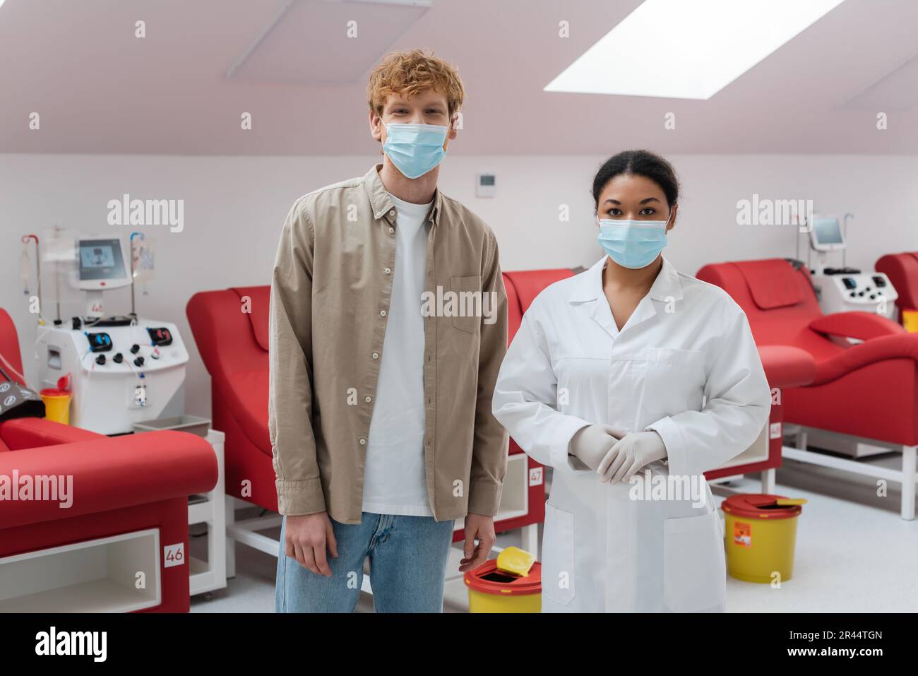 multiracial doctor and redhead volunteer in medical masks looking at ...