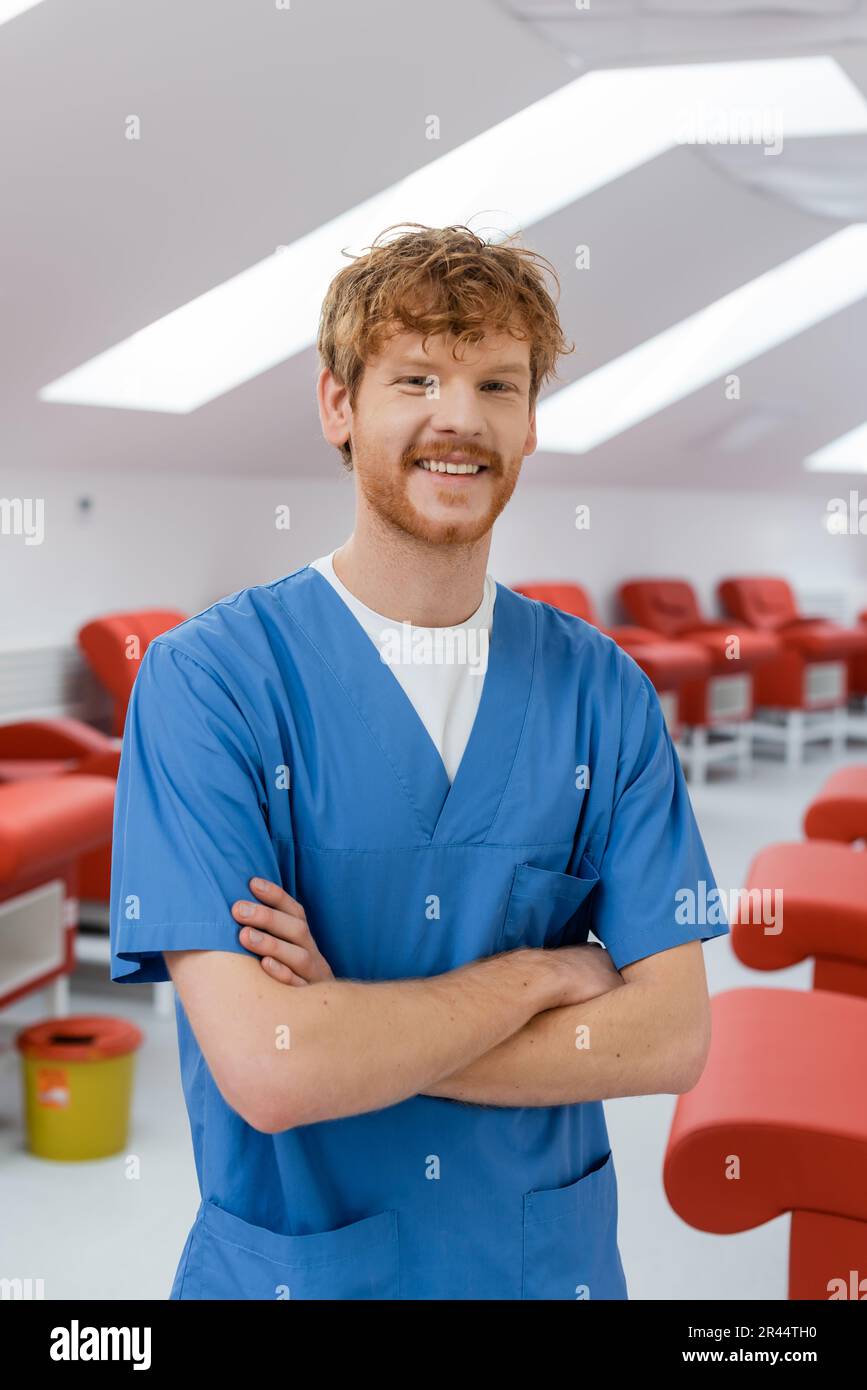 redhead healthcare worker in blue uniform standing with folded arms and ...